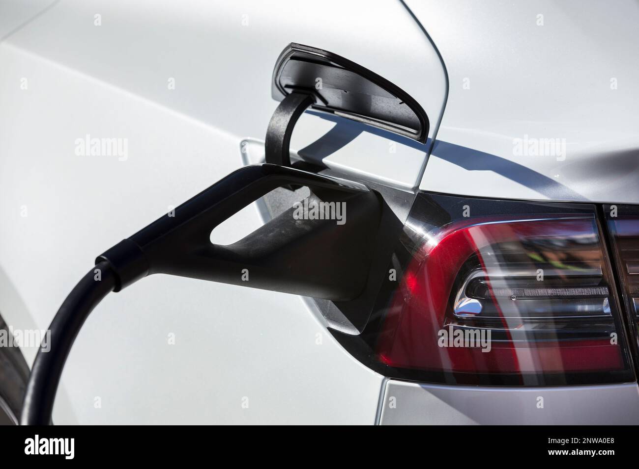 Detail of nozzle of electric charger plugged into back of white luxury ...