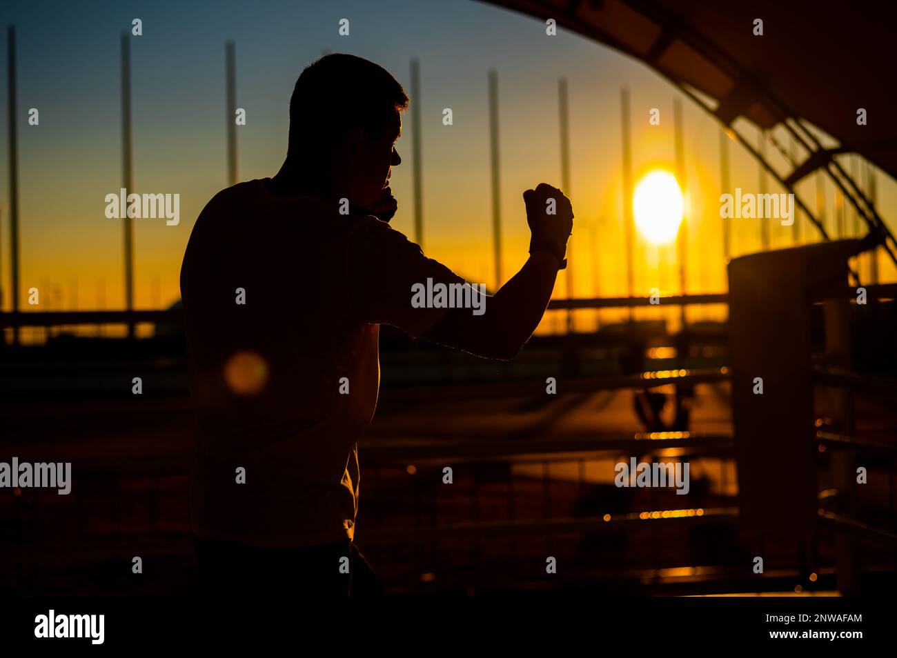 A man trains in boxing at the stadium at sunset. Athlete silhouette ...