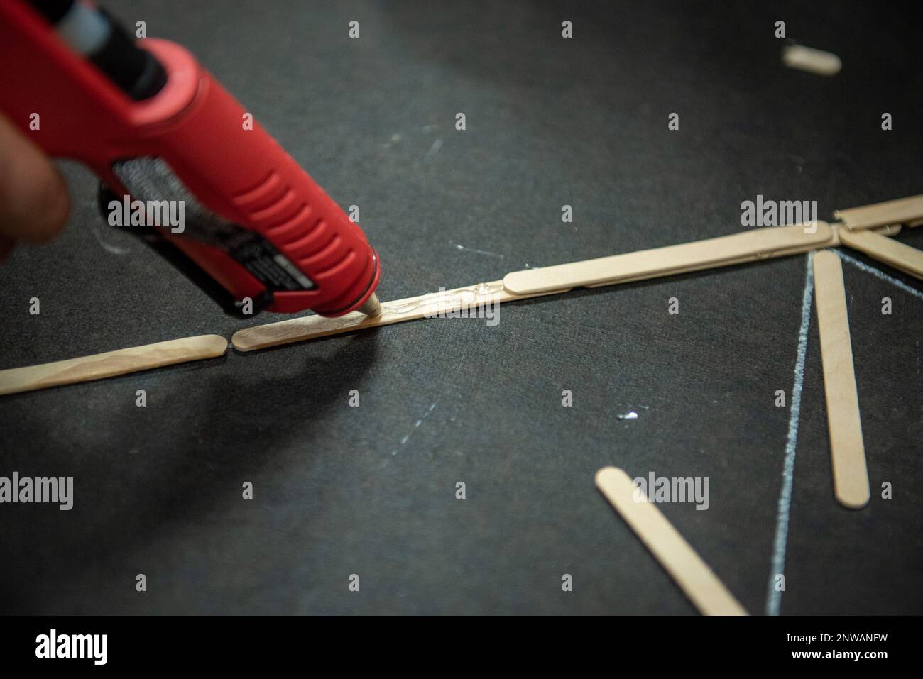 Joshua Sauls applies hot glue to a layer of popsicle sticks while ...