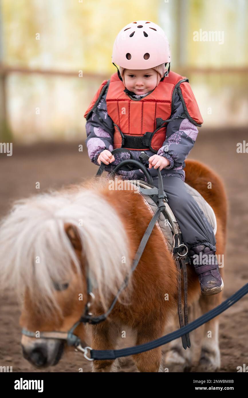 Little Child Riding Lesson. Three-year-old girl rides a pony and does ...