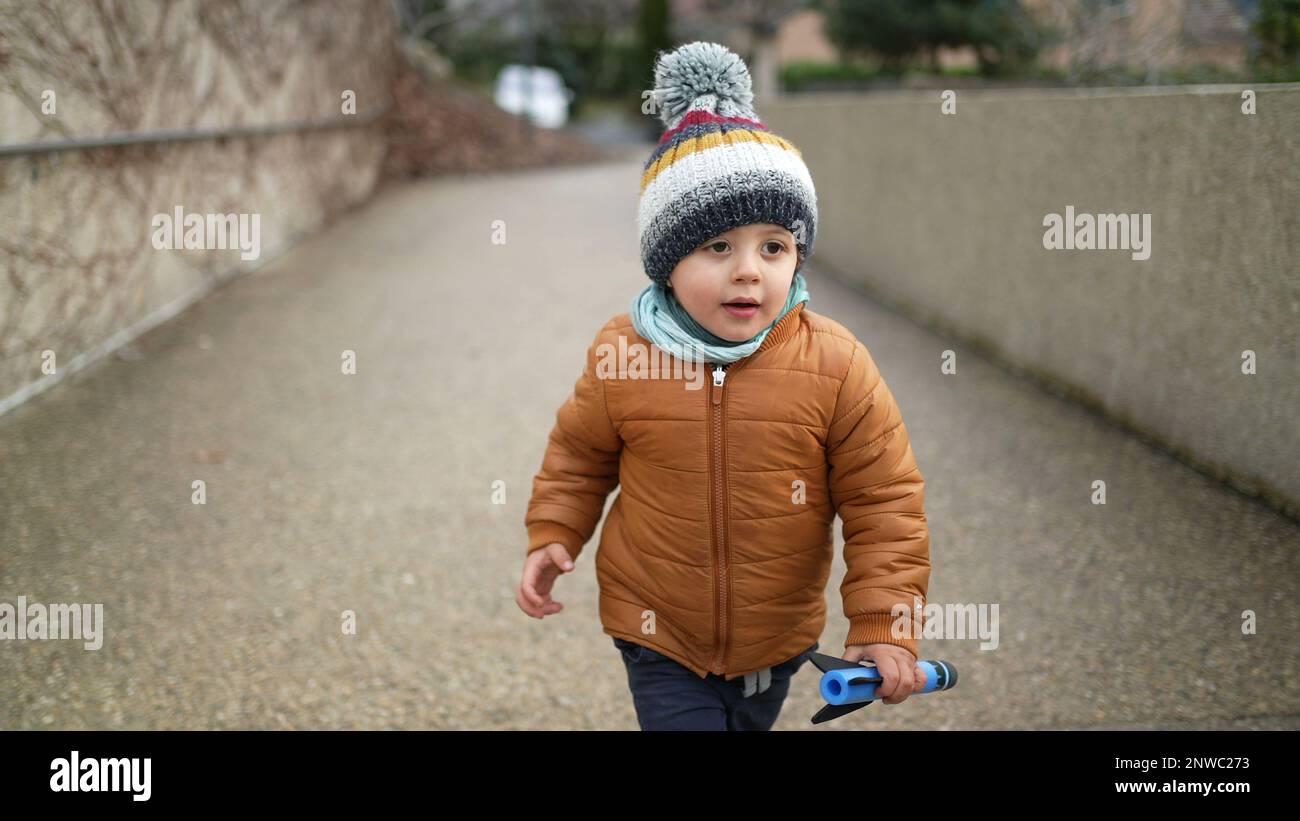 One cute little baby boy running outside in city park during winter ...