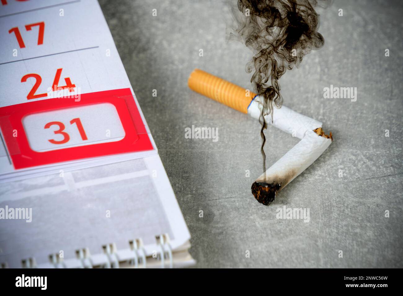 Black smoke coming from discarded cigarette.Background is calendar with ...