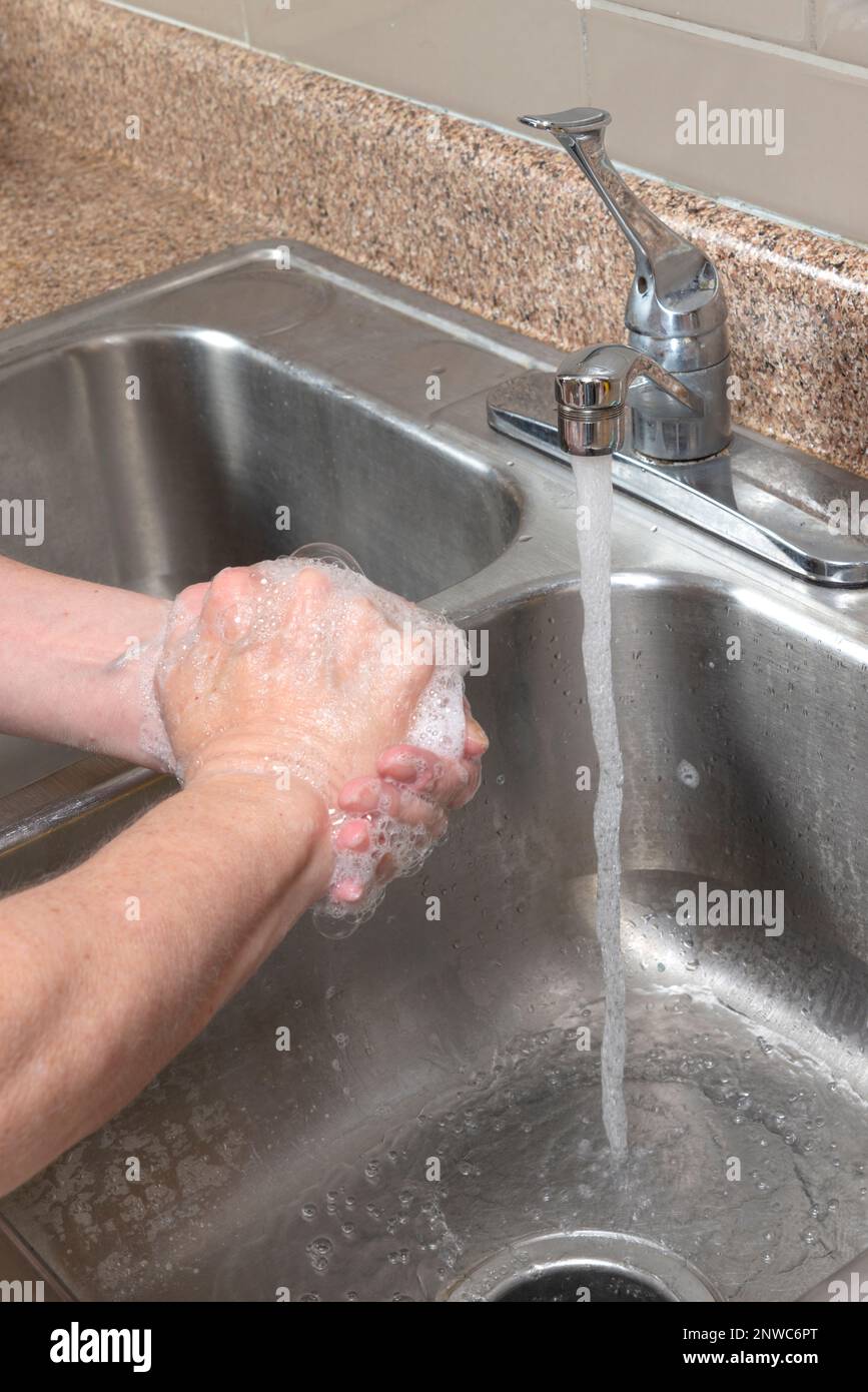 Vertical shot of a woman washing her hands in the kitchen sink with ...