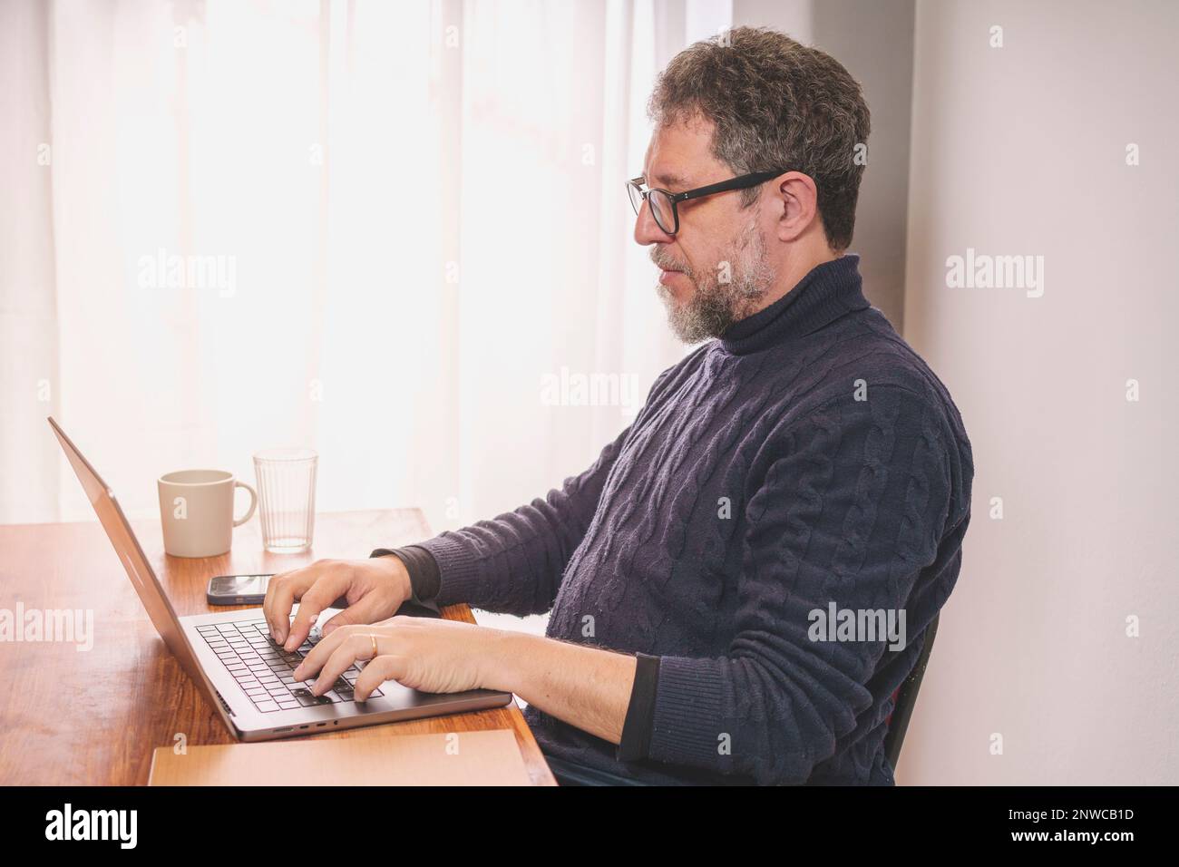 A middle-aged Caucasian man with grey beard is sitting at a desk and ...
