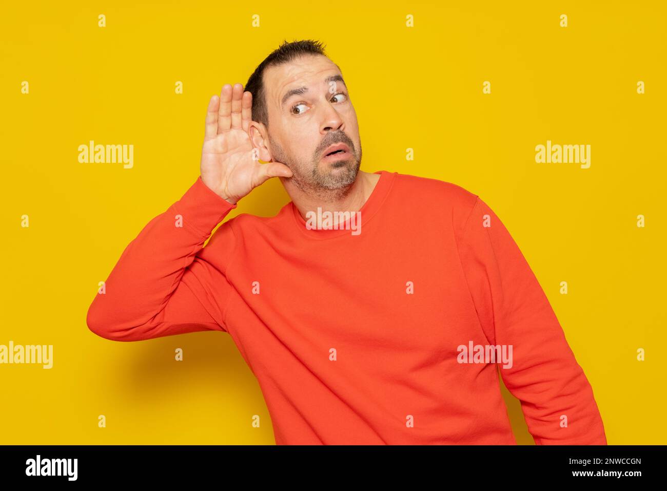 Listening Hispanic man holds his hand near his ear on a yellow ...