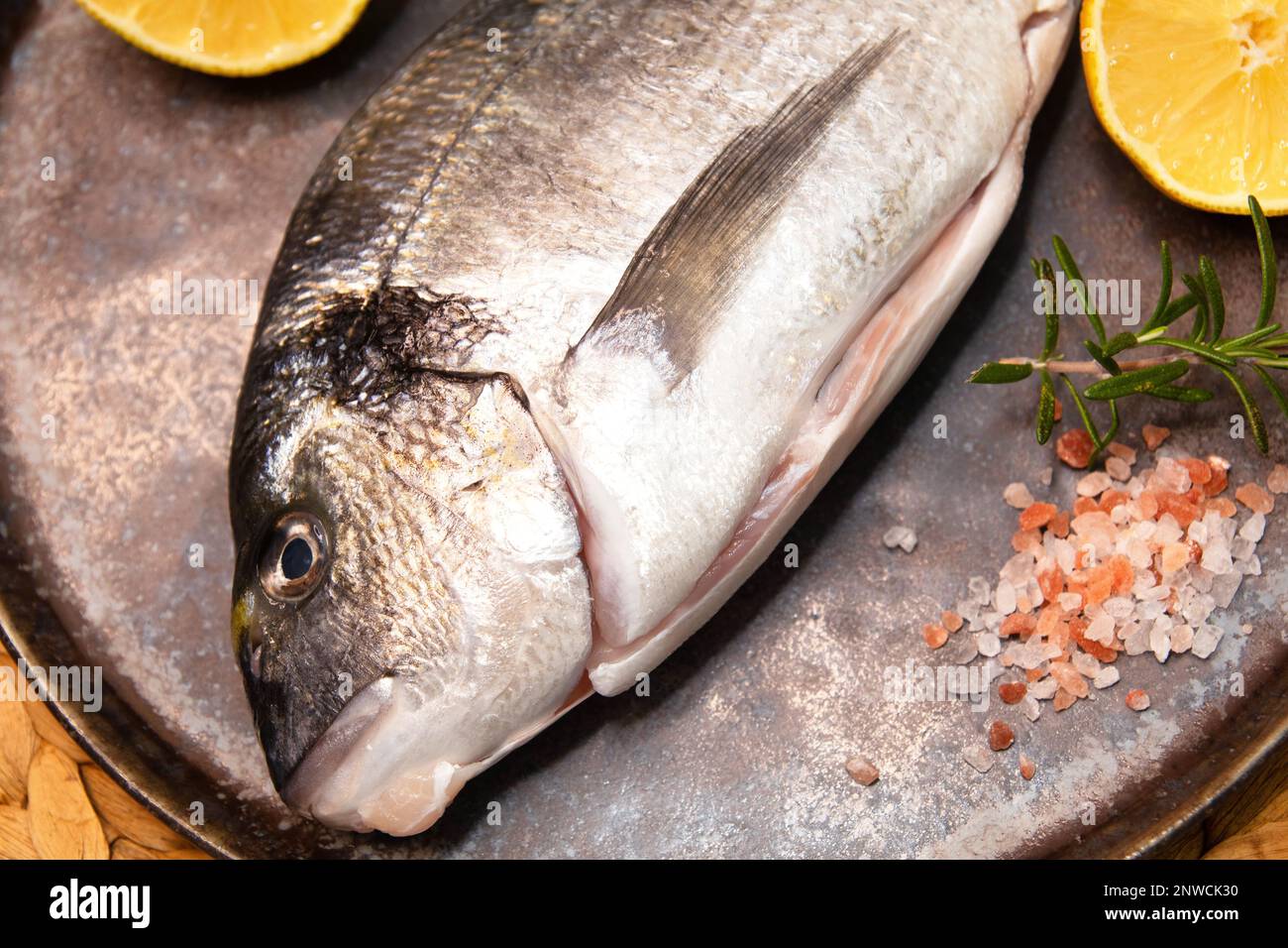 Fresh, raw sea bream on a plate with lemon slices, rosemary, and sea ...