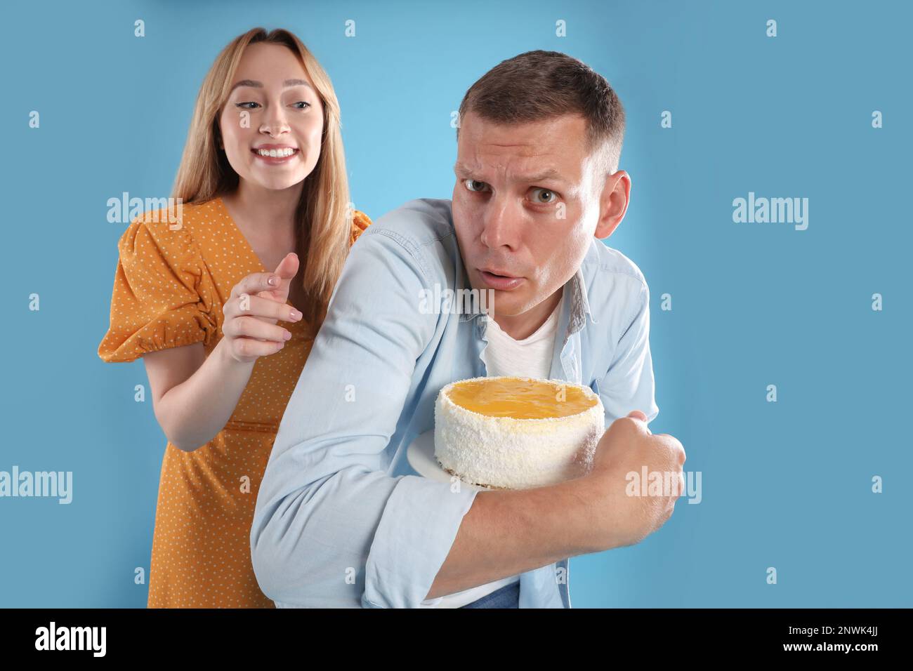Greedy man hiding tasty cake from woman on turquoise background Stock ...