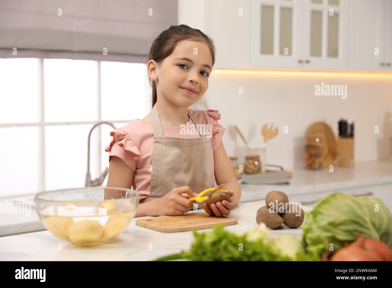 Little girl peeling potato at table in kitchen. Preparing vegetable ...