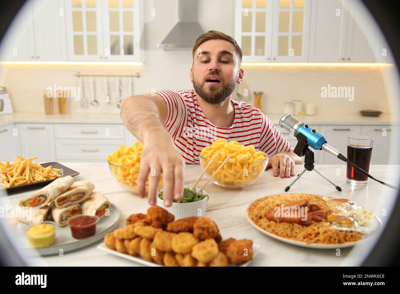 Food blogger eating near microphone at table in kitchen, view through ...