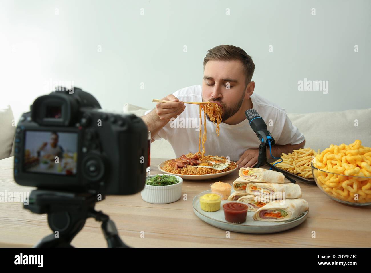 Food blogger recording eating show on camera against light background ...