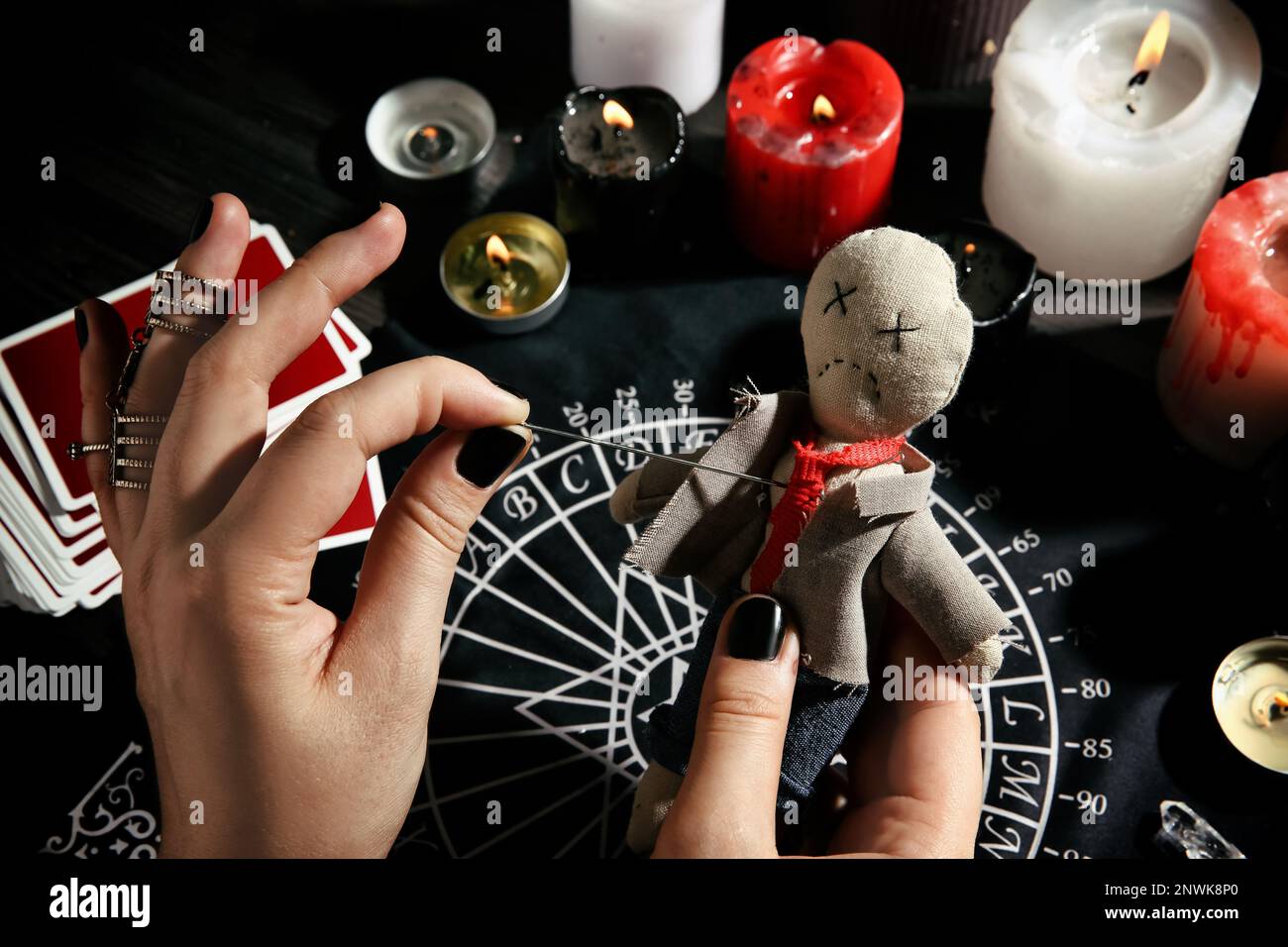 Woman stabbing voodoo doll with needle at table, closeup. Curse ...