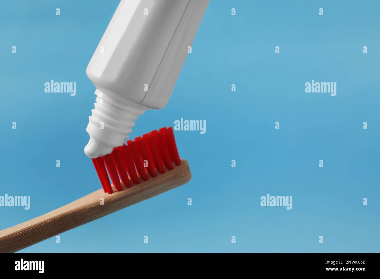 Squeezing toothpaste onto brush against light blue background, closeup ...