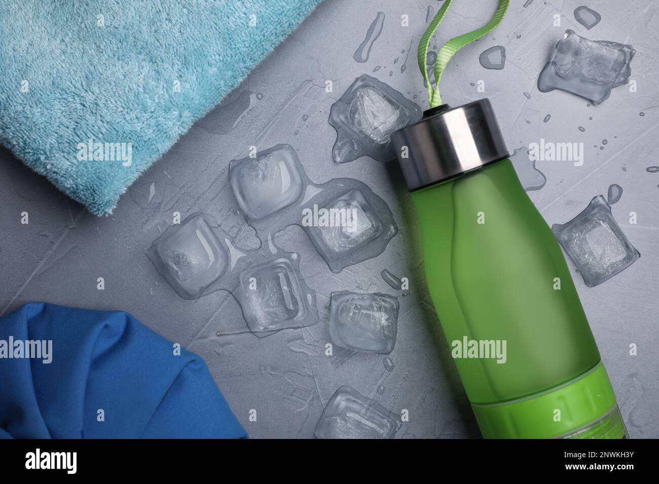 Bottle of water, ice cubes and towel on grey background, flat lay. Heat ...