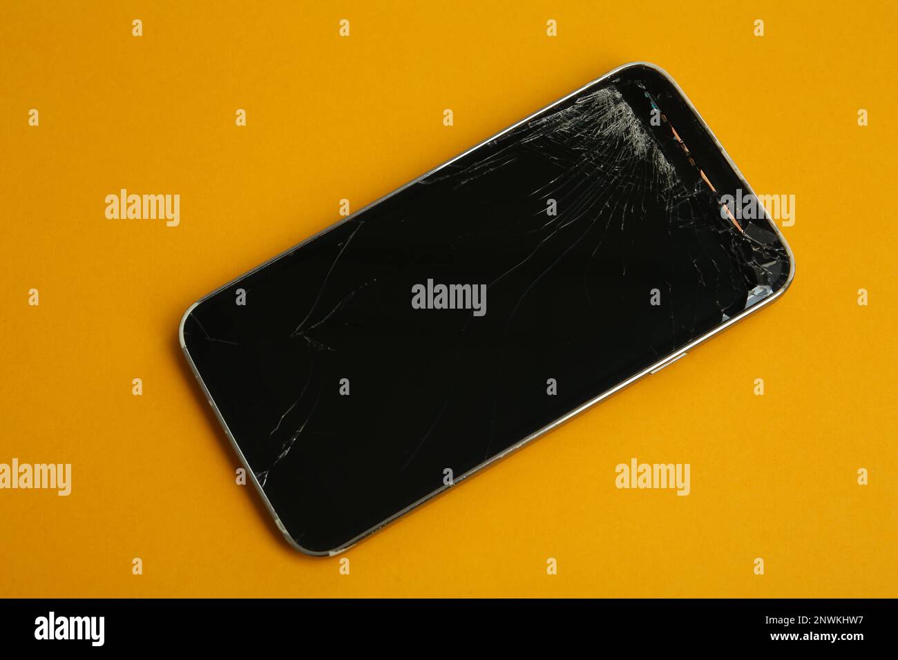 Smartphone with cracked screen on orange background, top view. Device ...