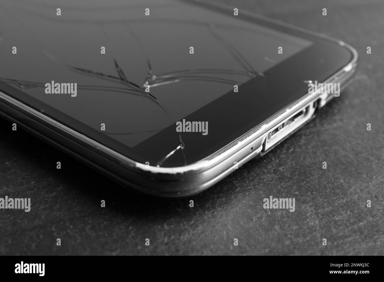 Smartphone with cracked screen on black table, closeup. Device repair ...