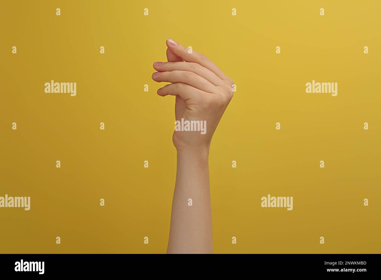 Woman showing thumb and index finger together on yellow background ...
