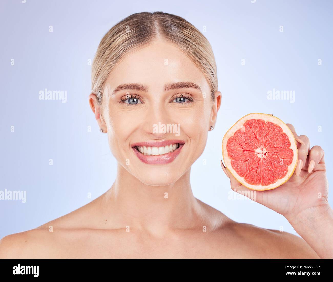 Face portrait, skincare and woman with grapefruit in studio isolated on a blue background. Food ...