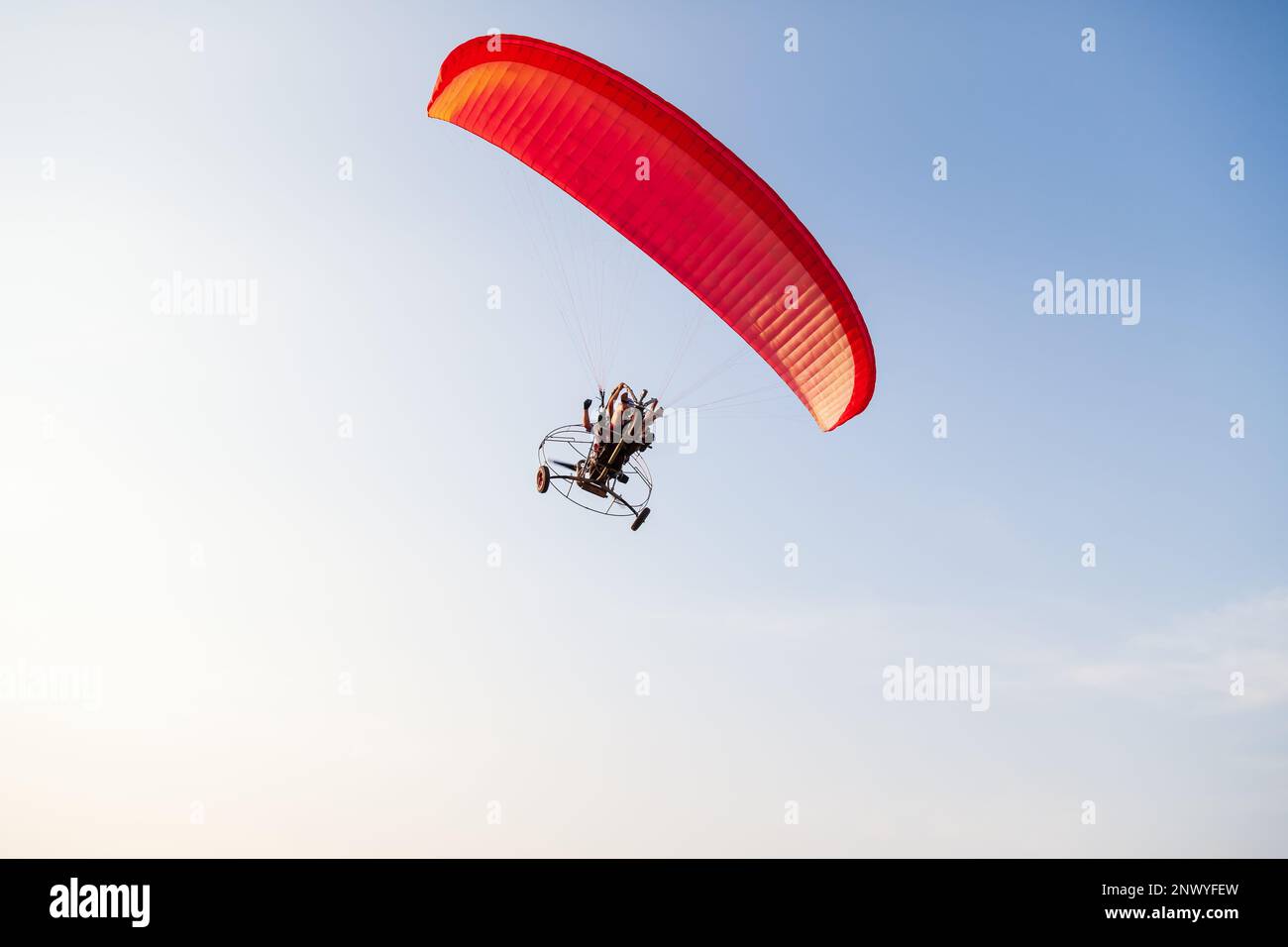 a red motorized paraglider in the blue sky flies with two passengers on ...