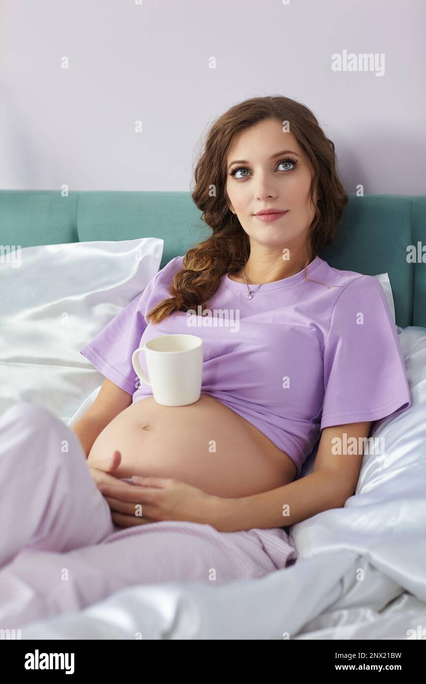 A pregnant woman lies in bed of her domestic bedroom. Female dressed in ...