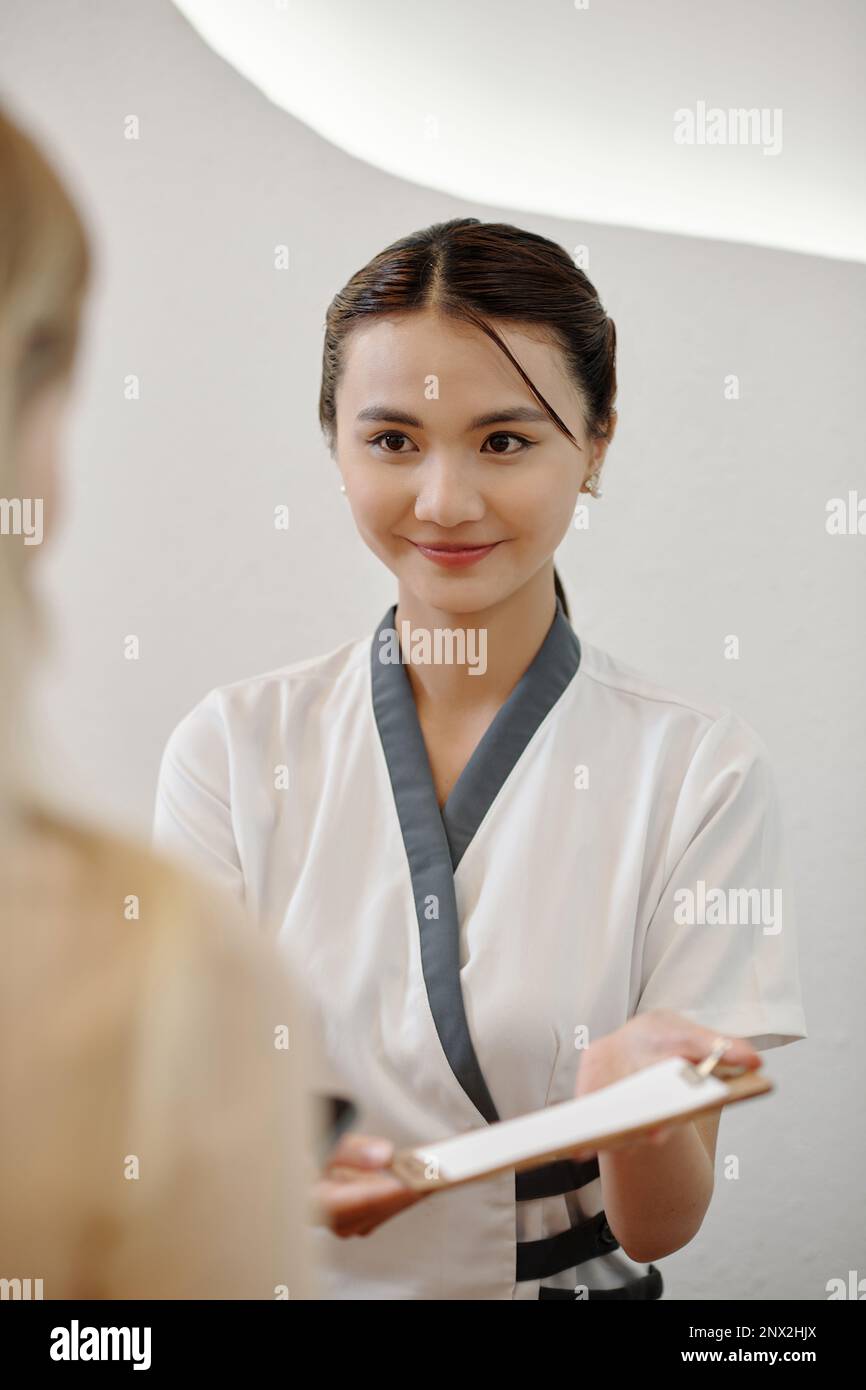 Smiling receptionist asking client to fill form Stock Photo - Alamy
