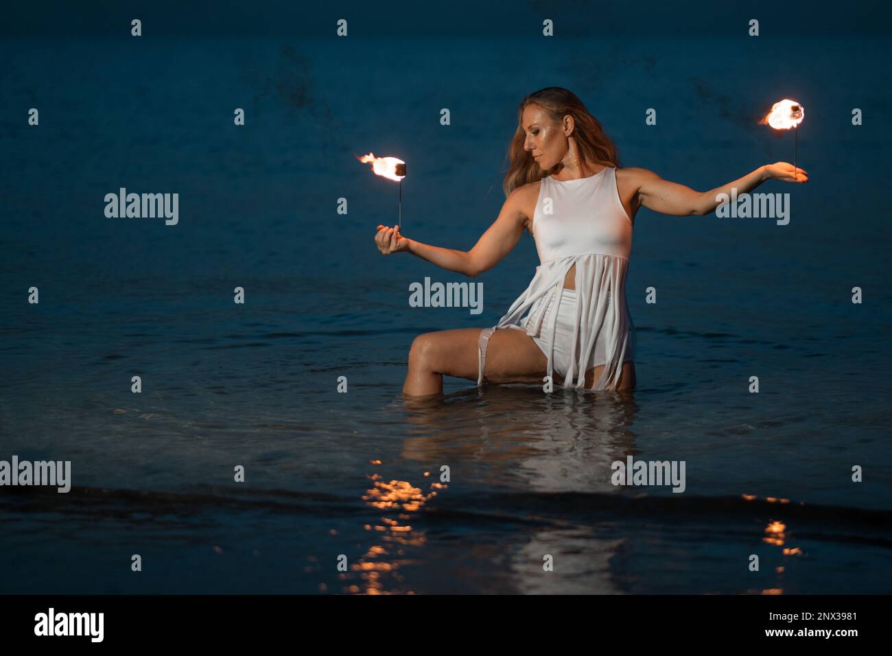 Caucasian woman dancing with fire in the water. Fire show at sea ...