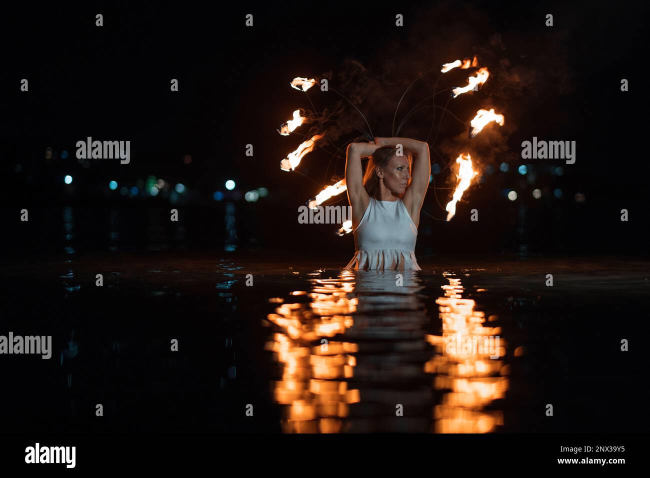 Caucasian woman dancing with fire in the water. Fire show at sea ...