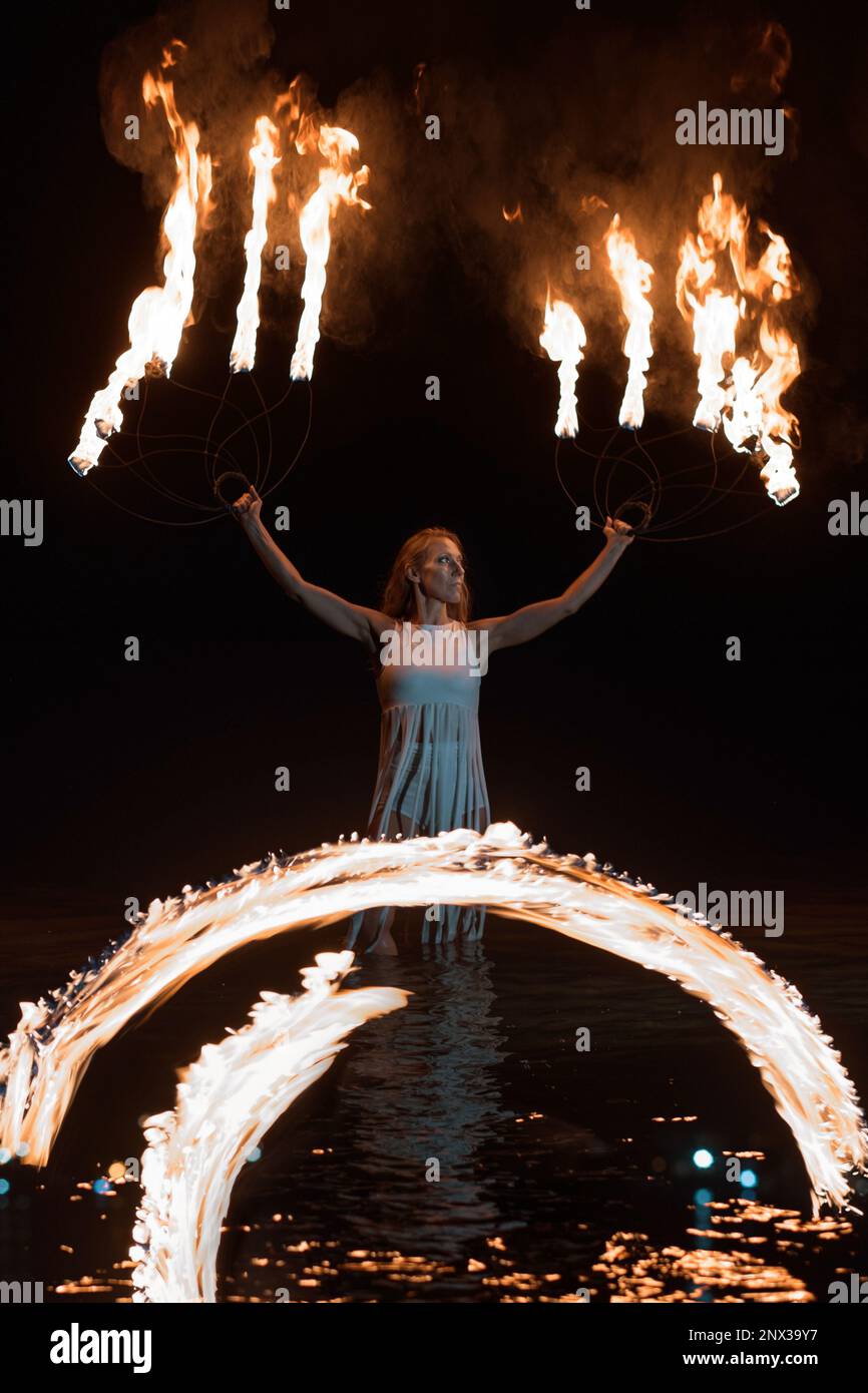 Caucasian woman dancing with fire in the water. Fire show at sea ...