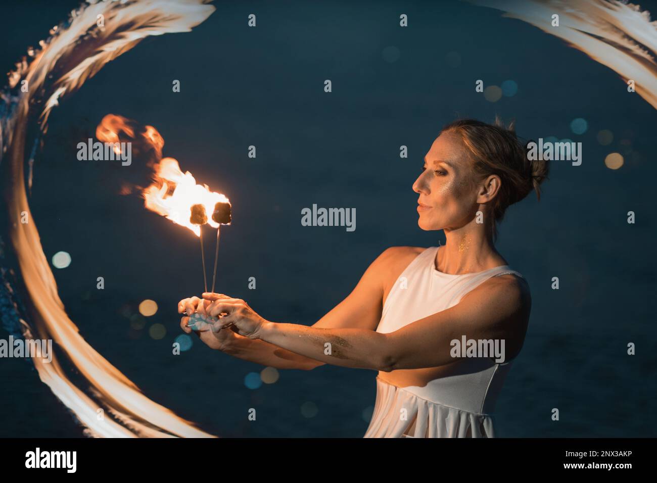 Caucasian woman dancing with fire in the water. Fire show at sea ...