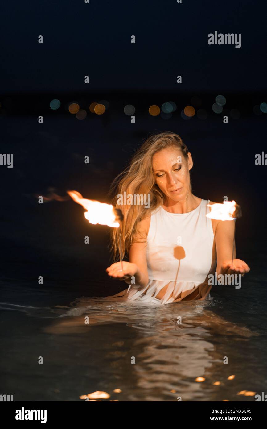Caucasian woman dancing with fire in the water. Fire show at sea ...