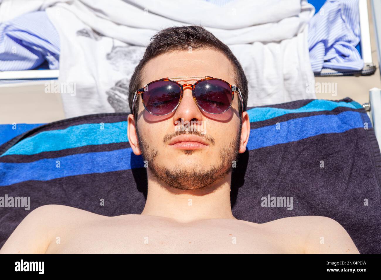 portrait of young man wearing sunglasses and tanning in summer on a ...