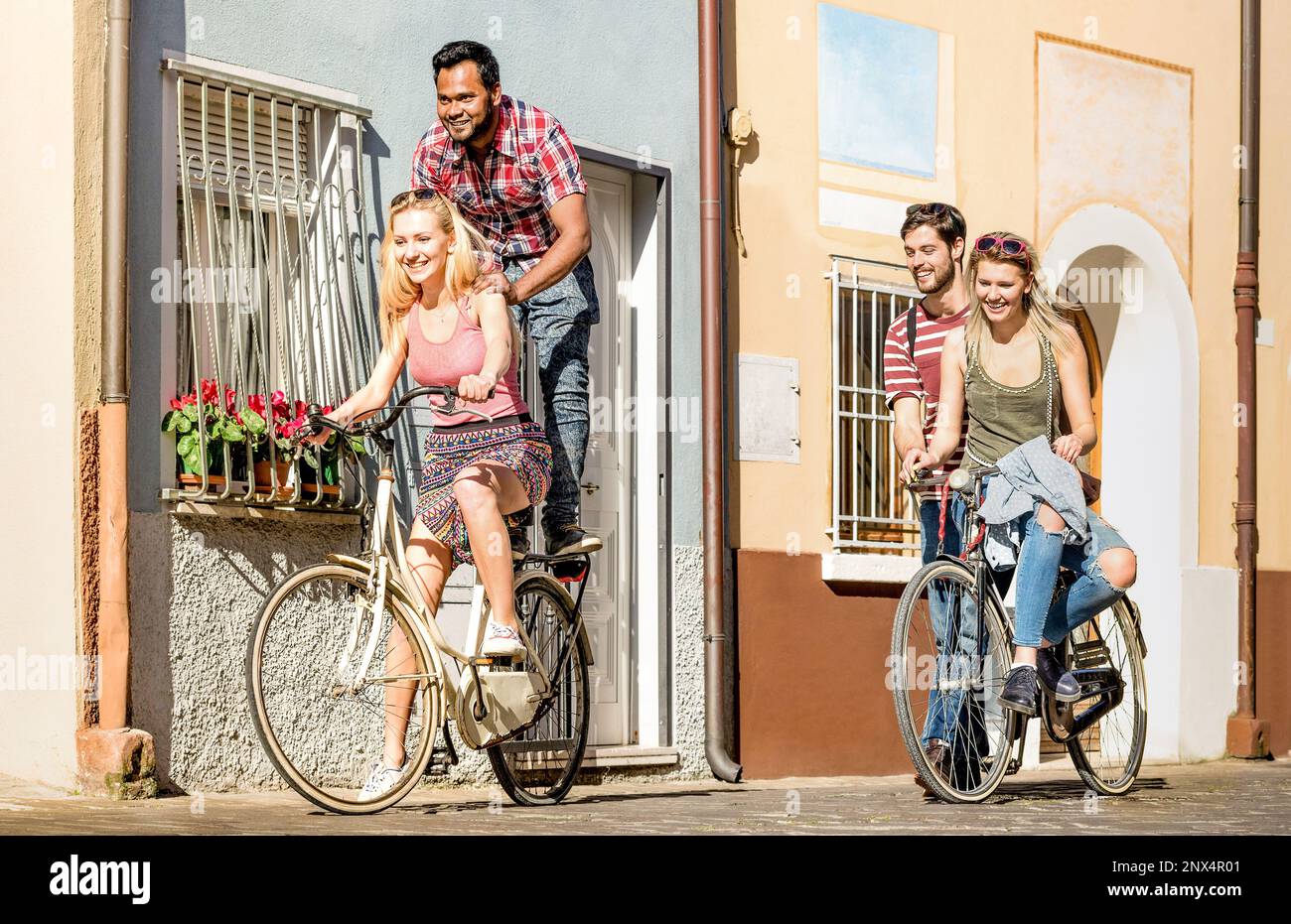 Happy multiracial friends couple having fun riding bicycle in city old ...