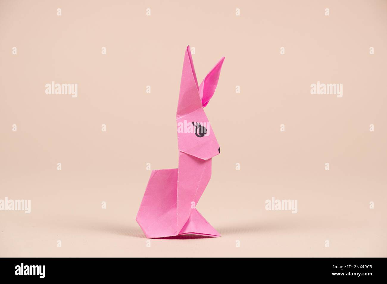 A pink origami rabbit on a beige background. Crafts for Easter, fold ...