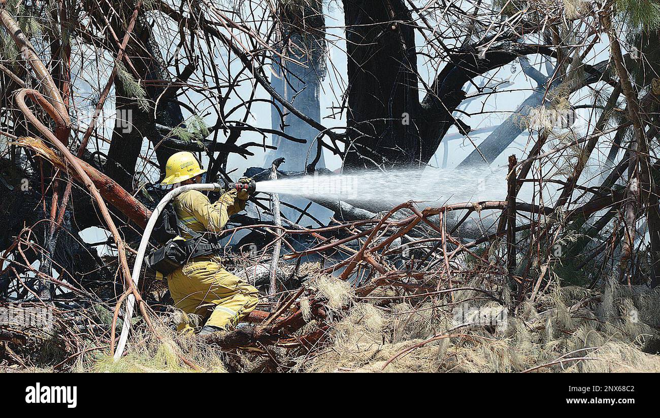 A firefighter works at extinguishing a brush fire on the south side of ...
