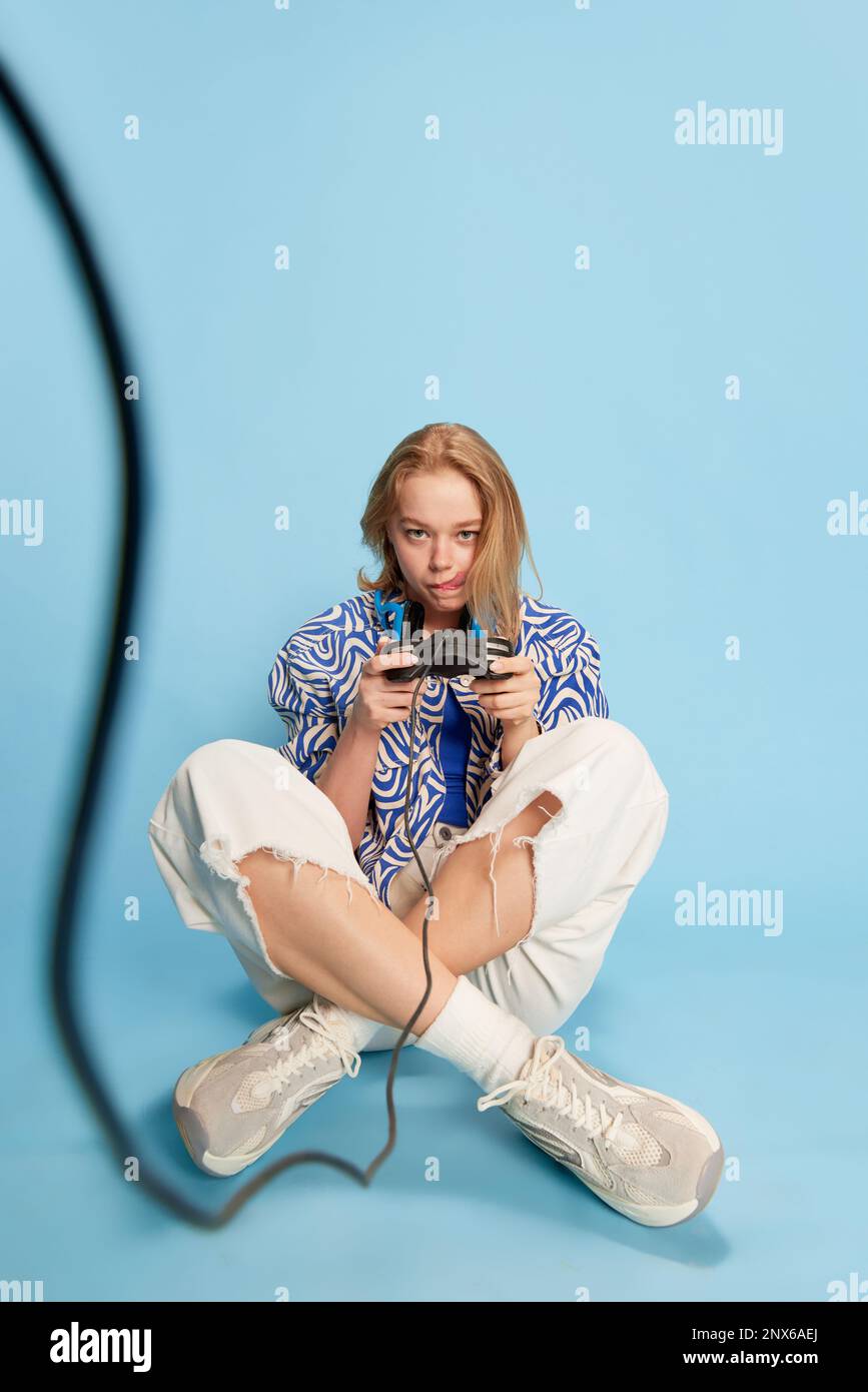 Young girl emotionally playing video game, sitting on floor over blue ...