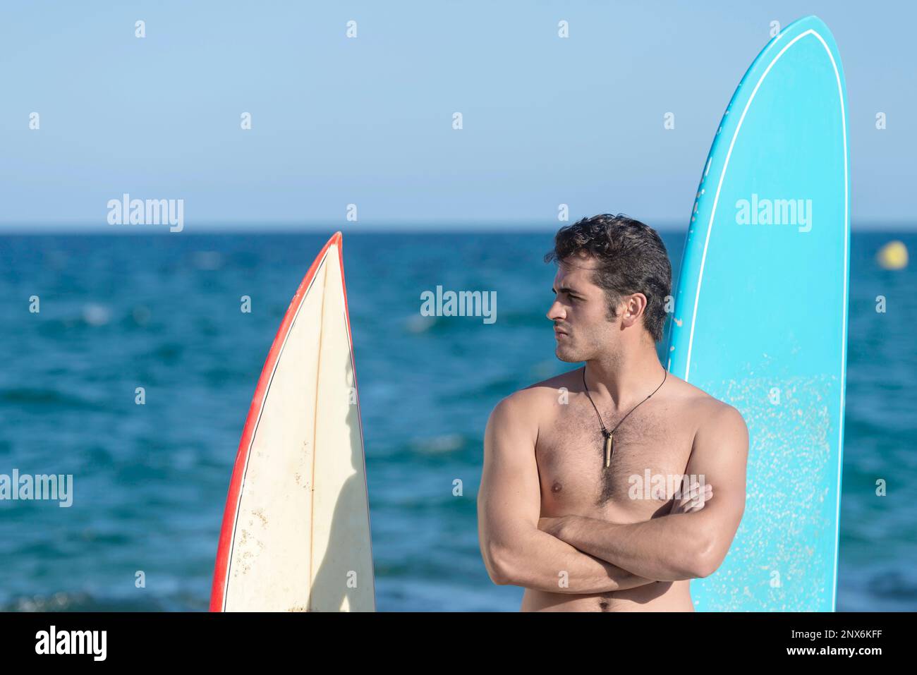 A Hispanic surfer guy standing on the beach in a swimsuit looking at ...