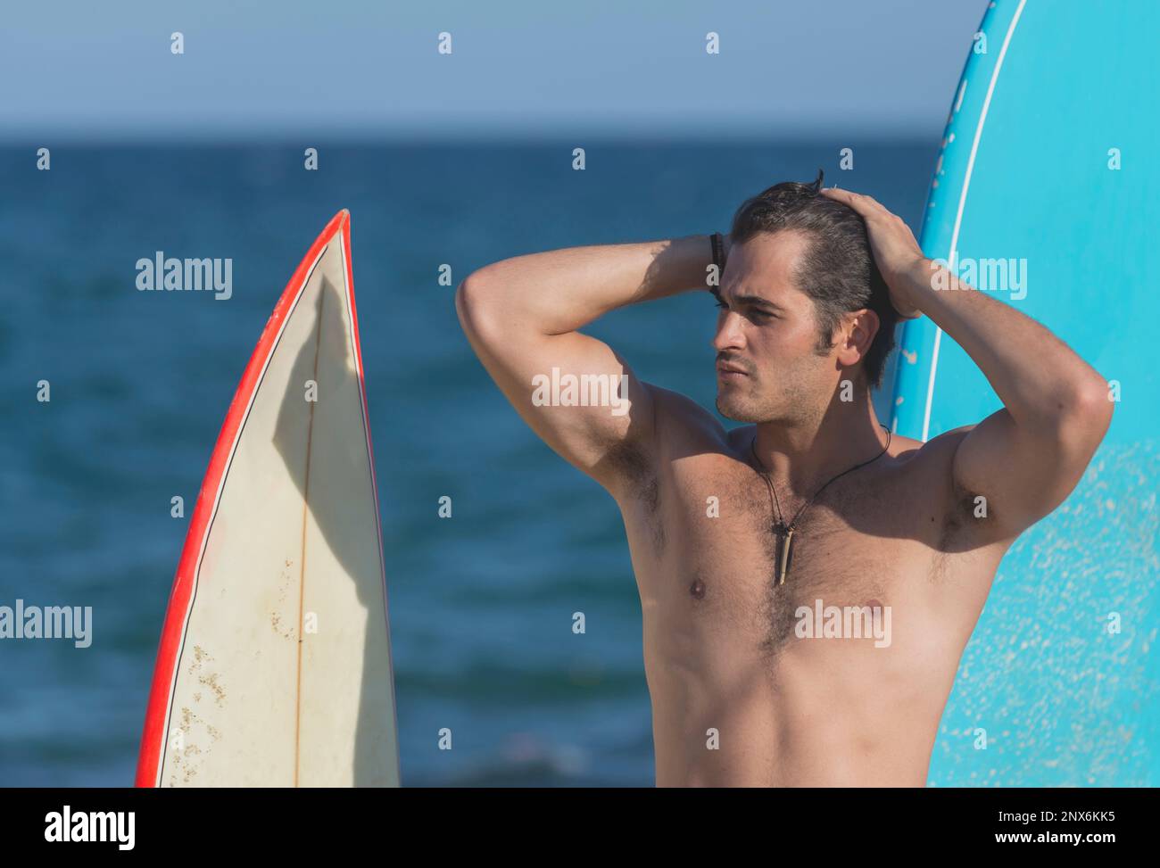 A Hispanic surfer guy standing on the beach in a swimsuit looking at ...