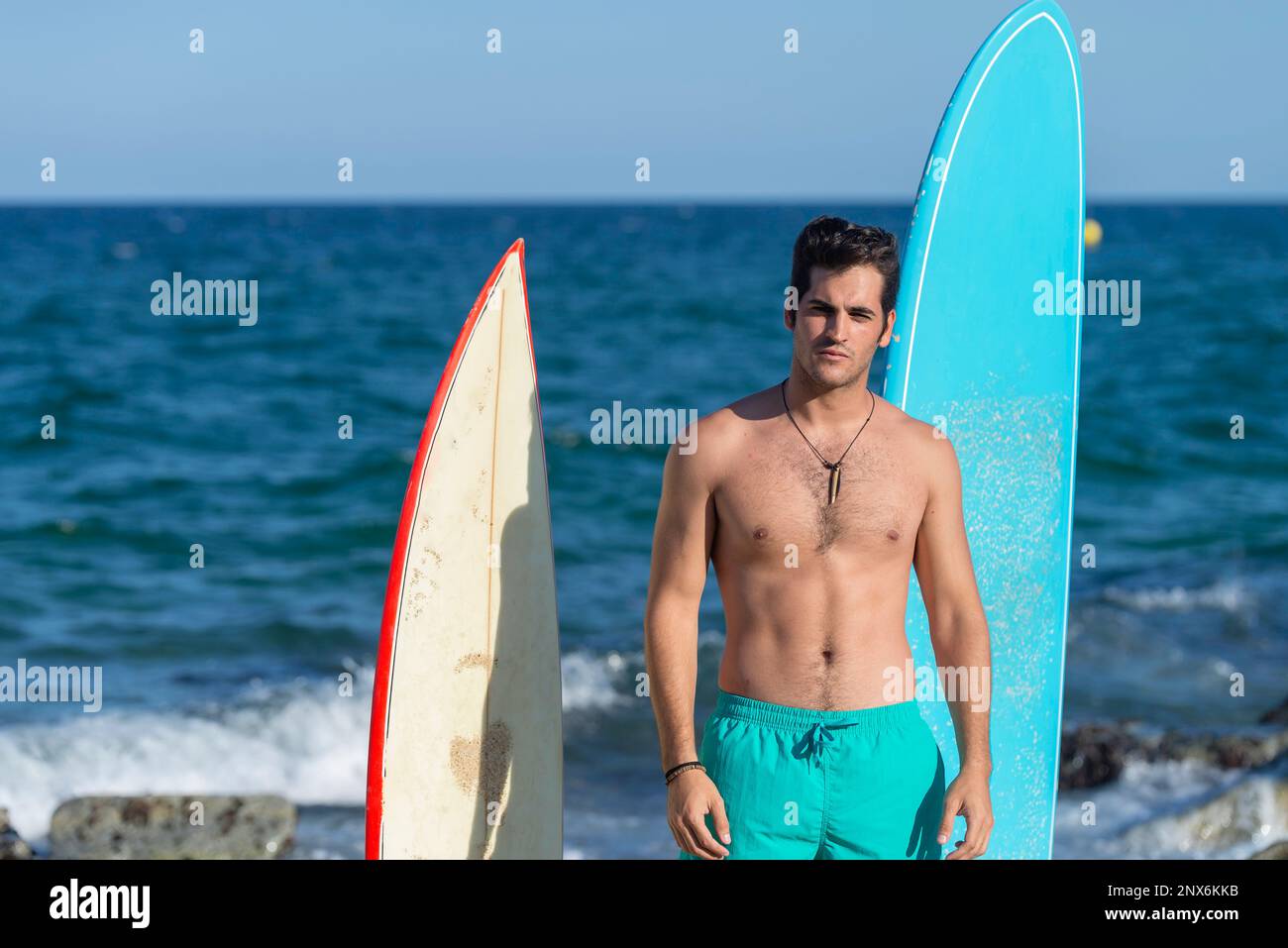 A Hispanic surfer guy standing on the beach in a swimsuit looking at ...
