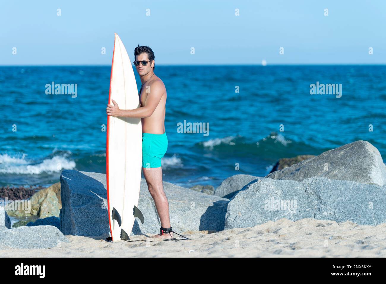 Hispanic surfer boy standing on the beach in neoprene holding his blue surfboard at sunset Stock ...