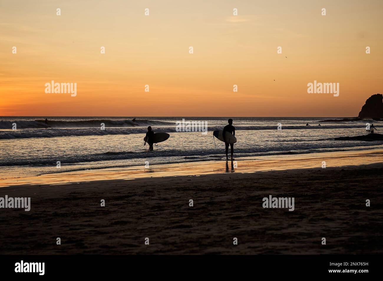 two people walking along a sandy beach, each carrying a long surfboard ...