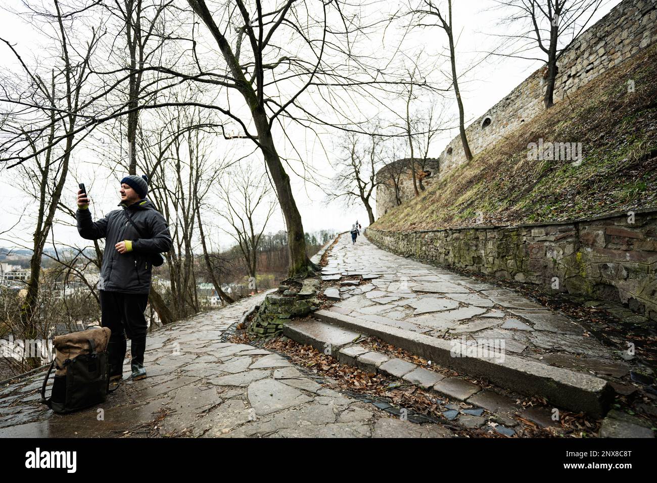 Man tourist with backpack look at phone, stand on wet path to an ...