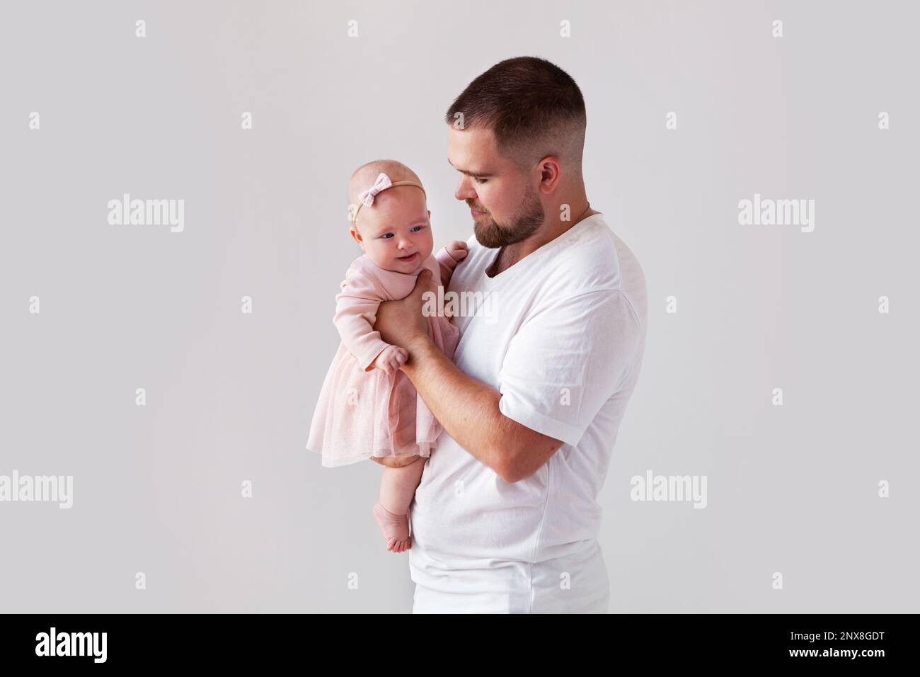 Portrait young Dad holding newborn baby girl in pink dress on white ...