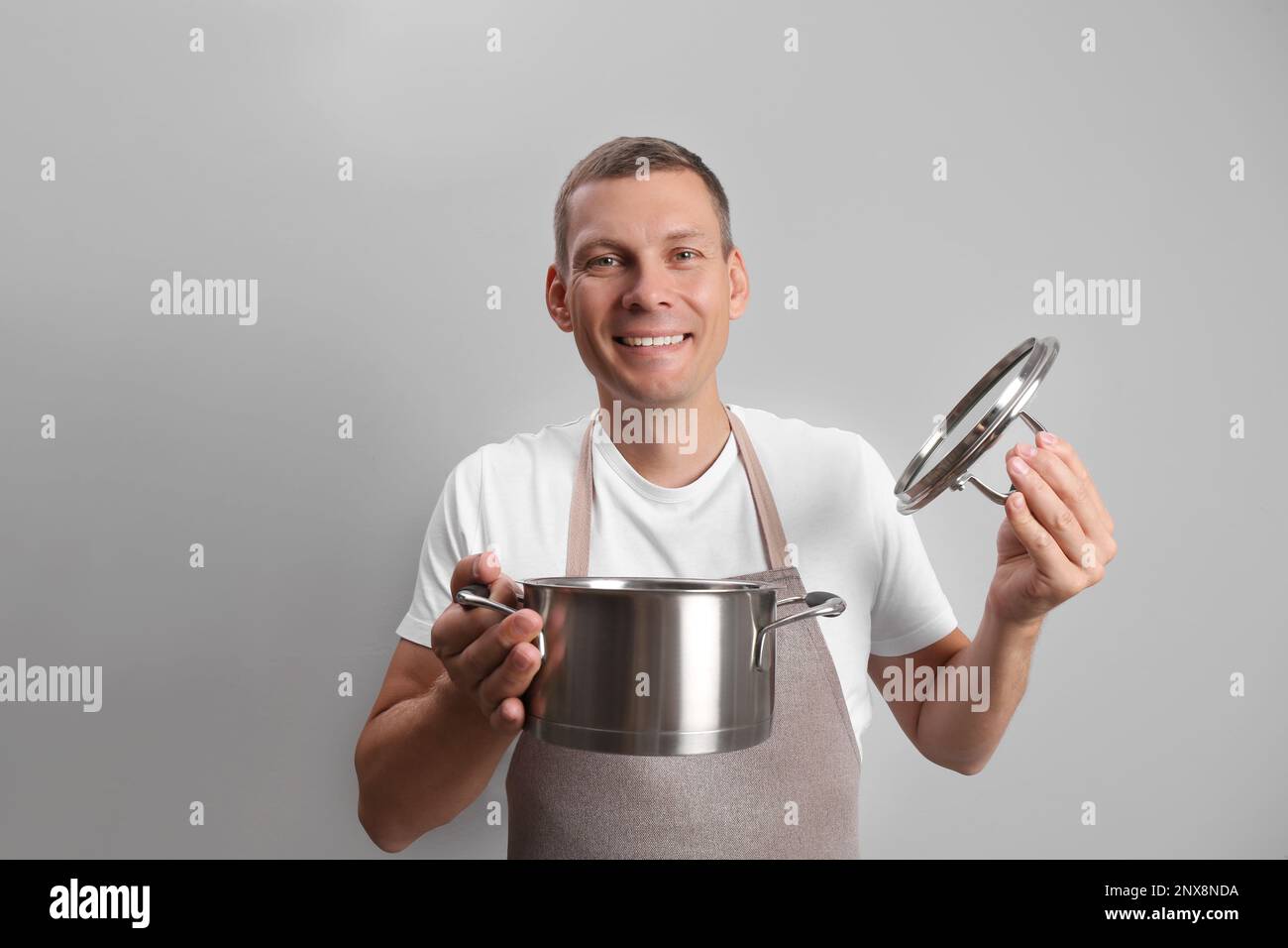 Happy man with cooking pot on light grey background Stock Photo - Alamy