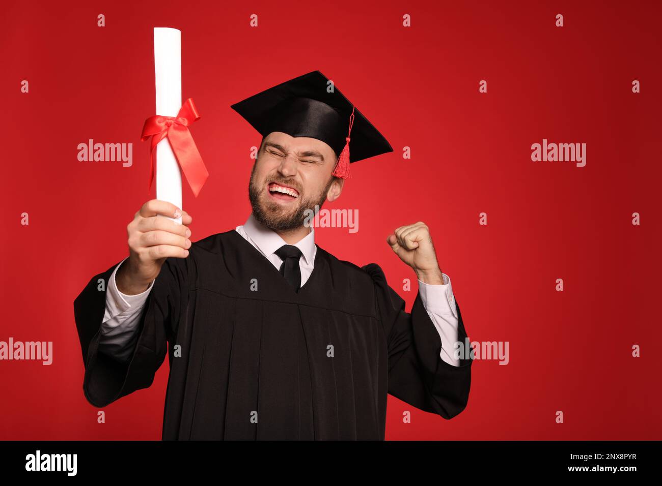Emotional student with graduation hat and diploma on red background ...