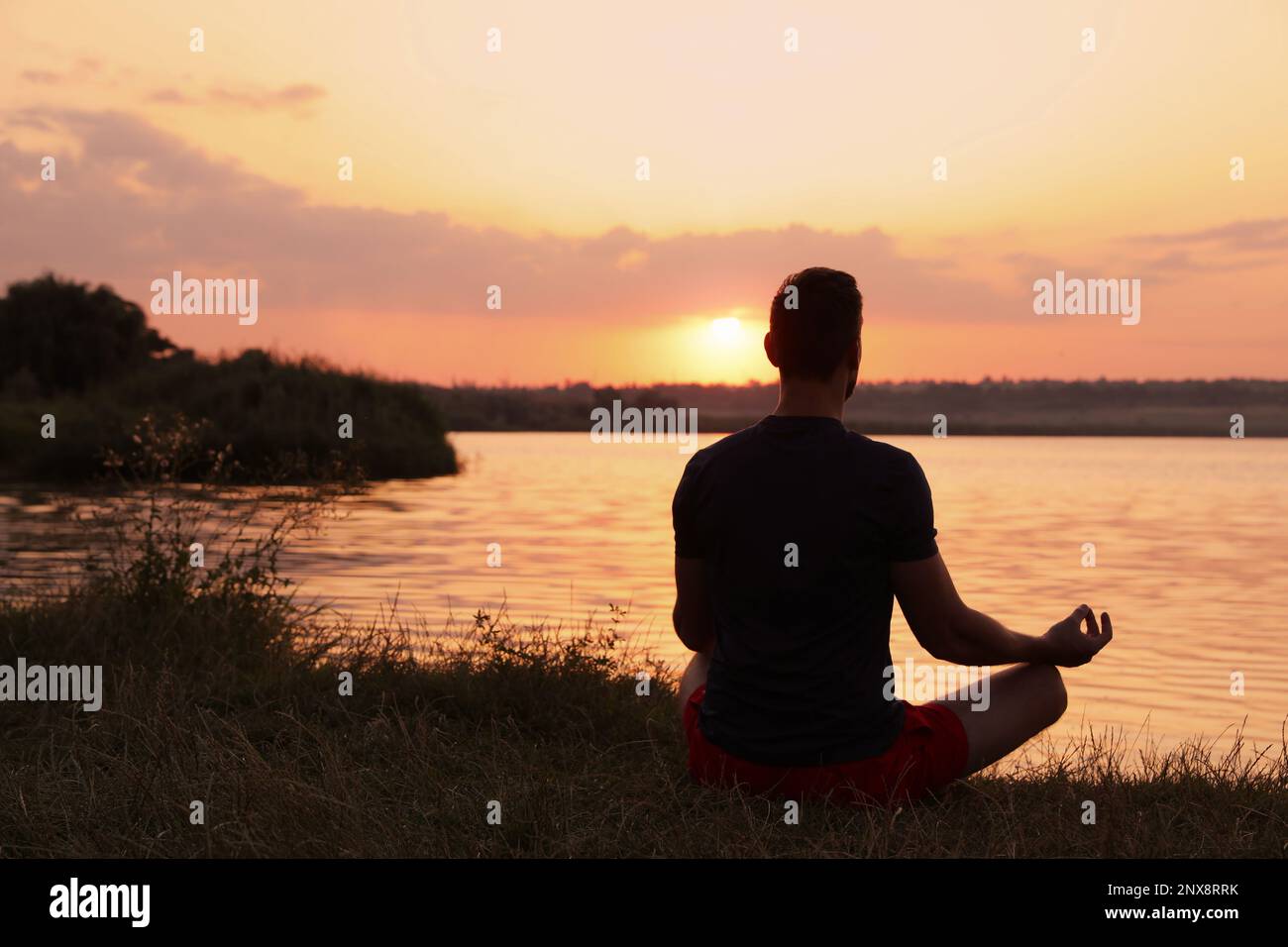 Man meditating near river at sunset, back view. Space for text Stock ...