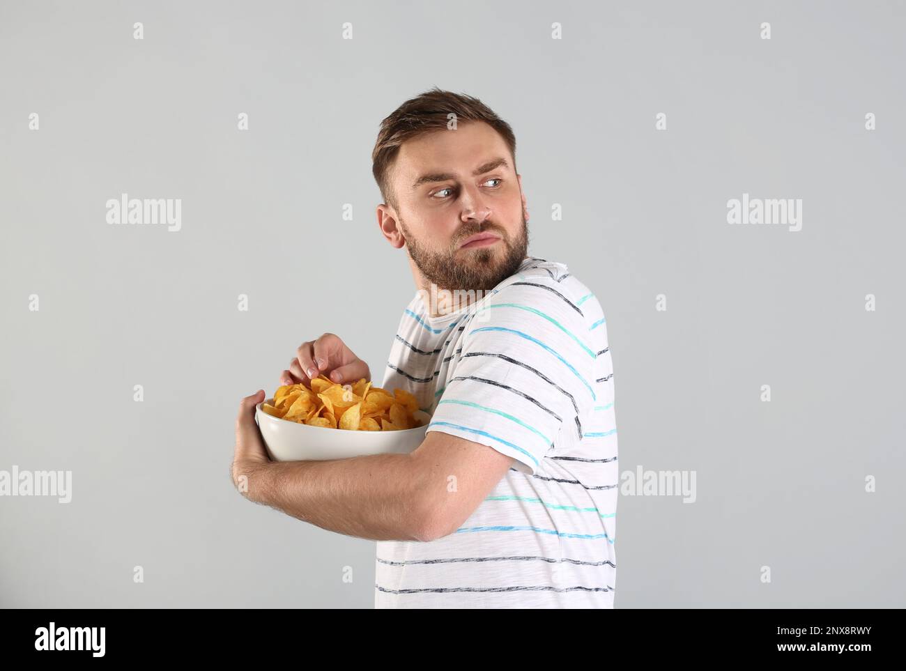 Greedy young man hiding bowl with chips on light grey background Stock ...