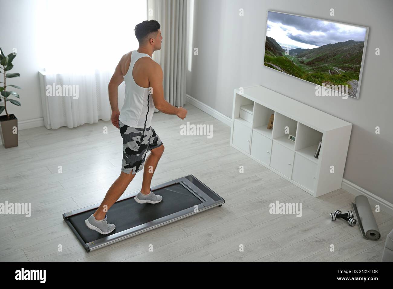 Sporty man training on walking treadmill and watching TV at home Stock ...