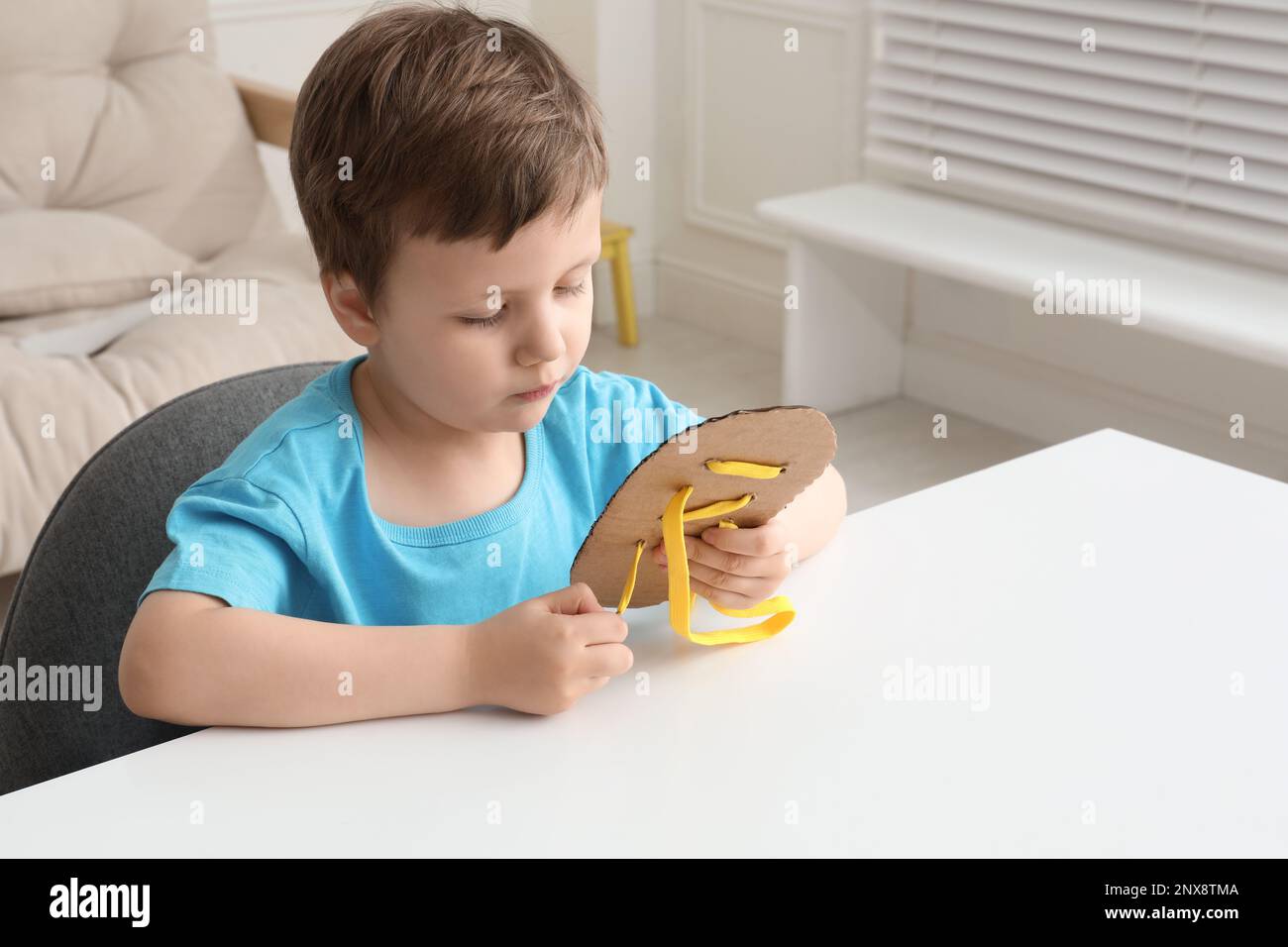 Little boy tying shoe lace using training cardboard template at white ...