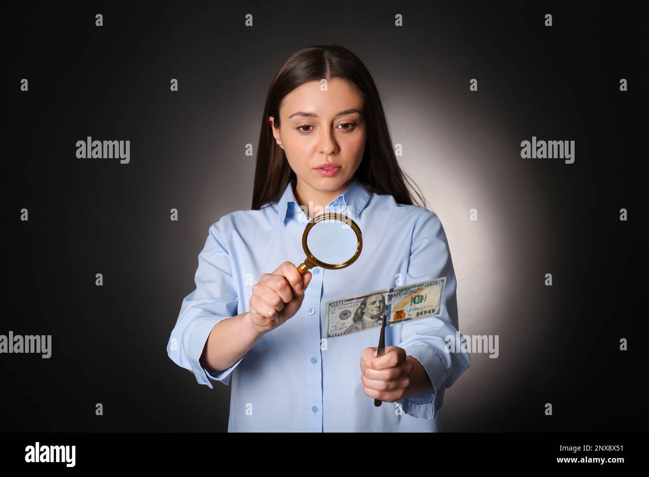 Expert authenticating 100 dollar banknote with magnifying glass against ...