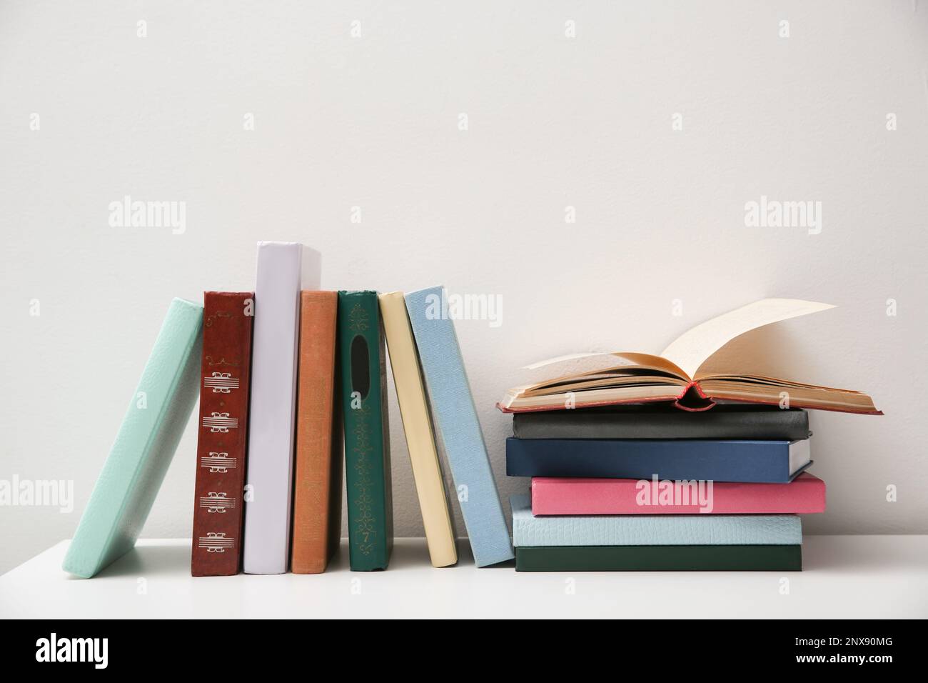 Different books on white table near light grey wall Stock Photo - Alamy