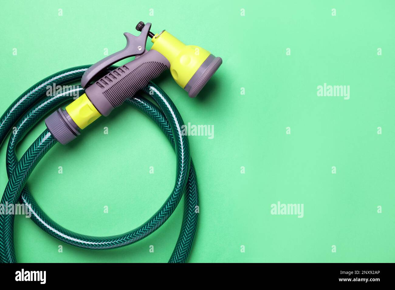Watering hose with sprinkler on green background, top view. Space for ...